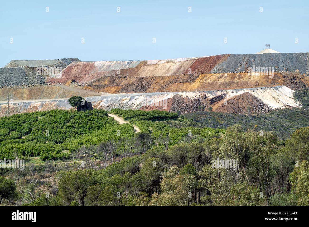 A vast expanse of an open-pit mine situated on a hillside covered in a ...