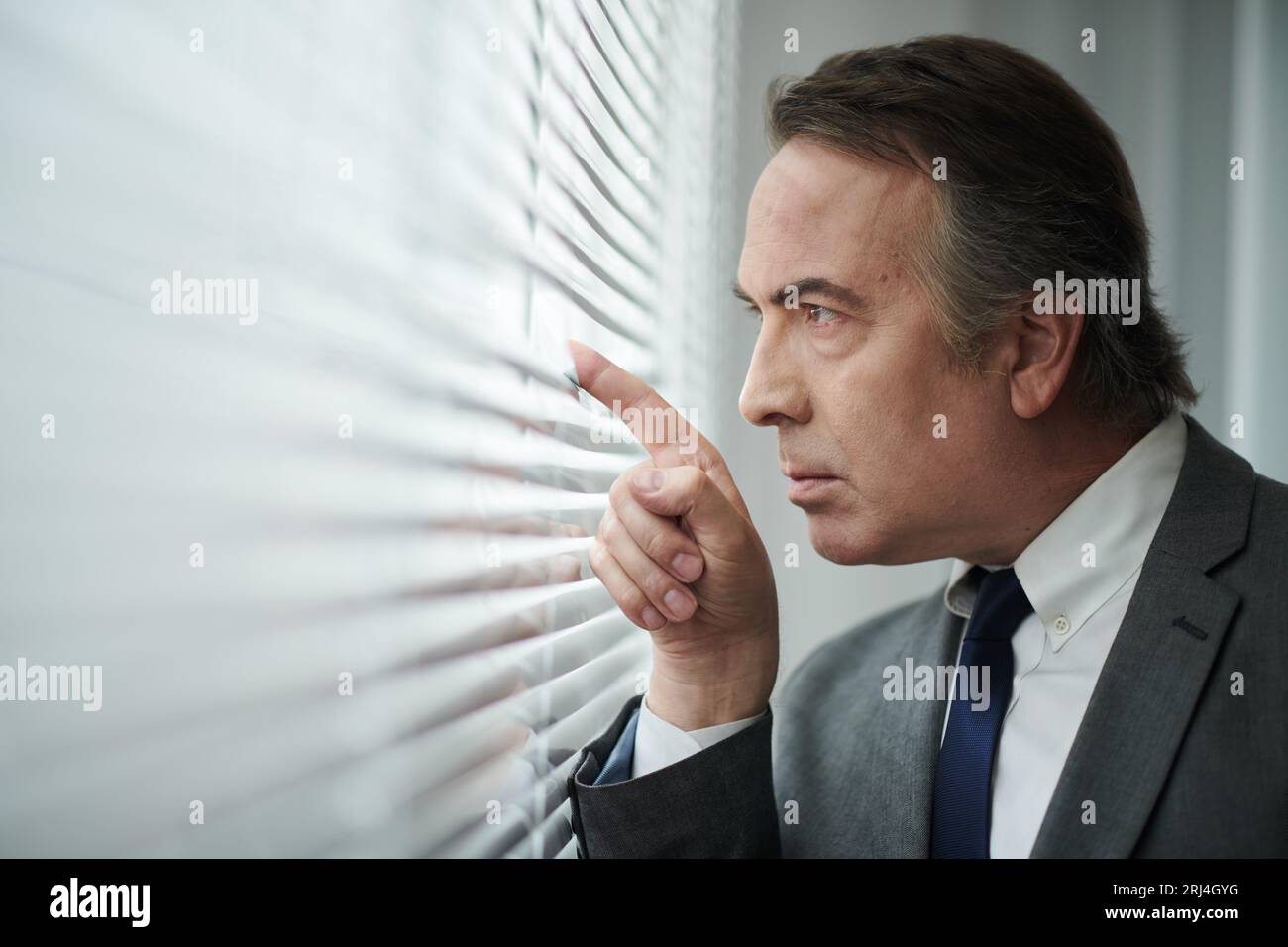 Curious mature businessman peaking through window blinds Stock Photo ...