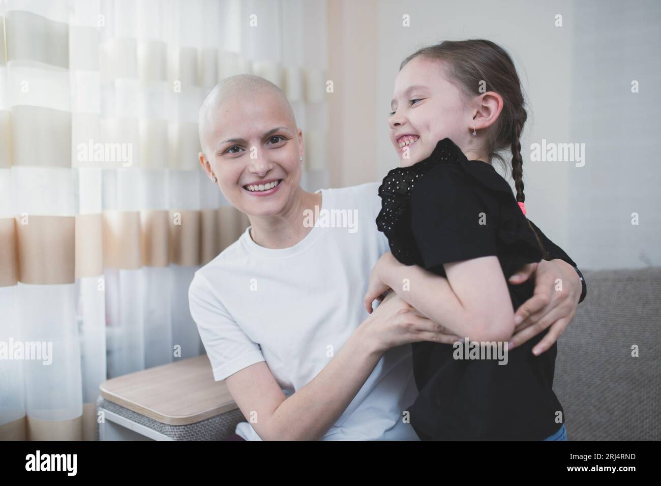 Young smiling bald woman with cancer spending time with her kid at home ...