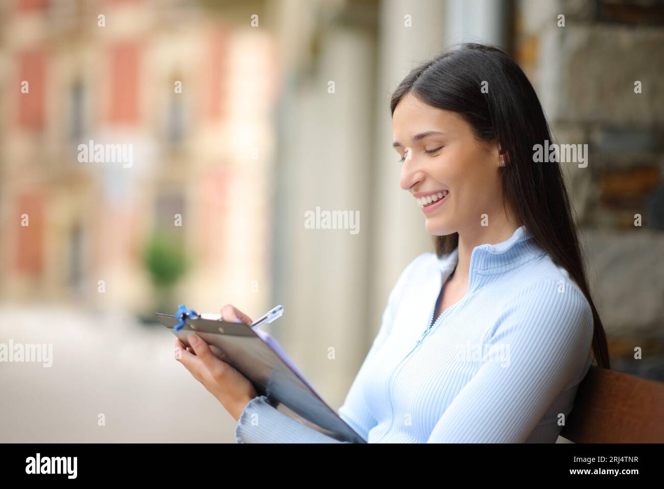 Happy woman filling survey sitting on a bench in the street Stock Photo ...