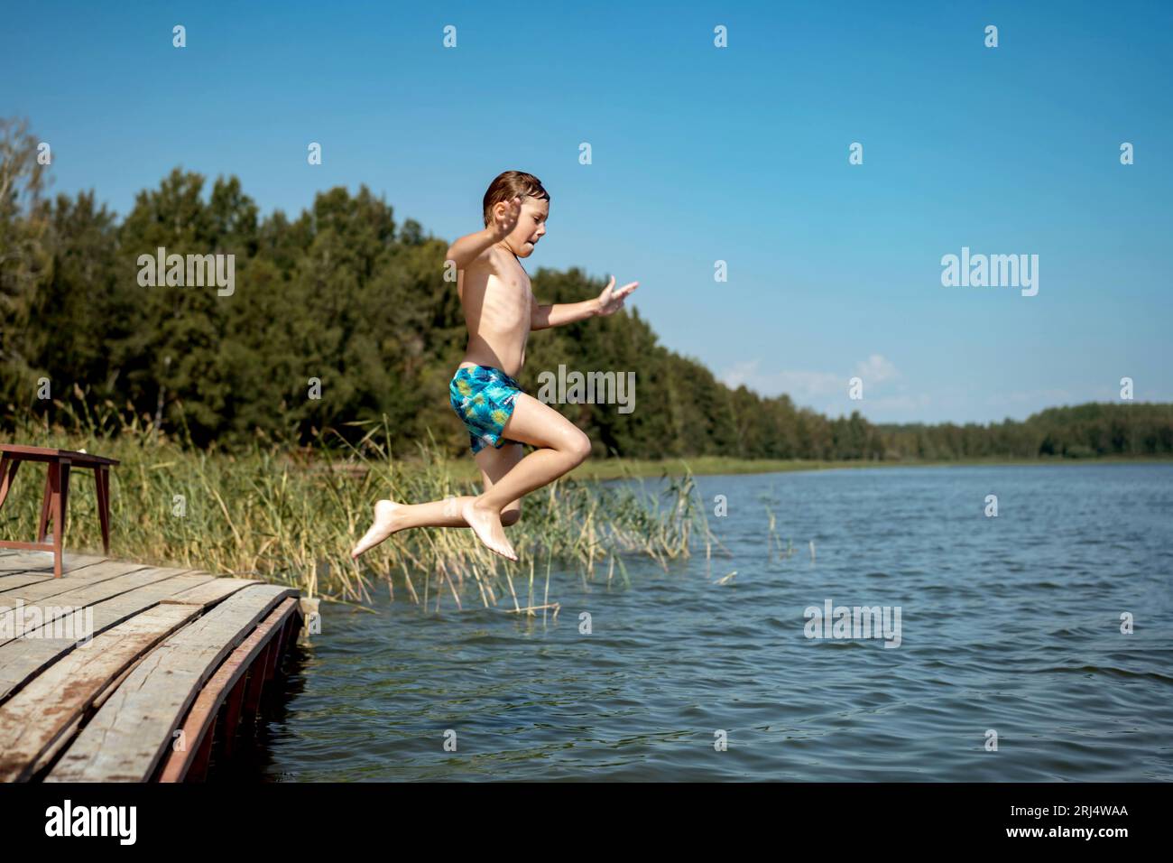 cute caucasian boy jumping from wooden pier diving into lake in ...