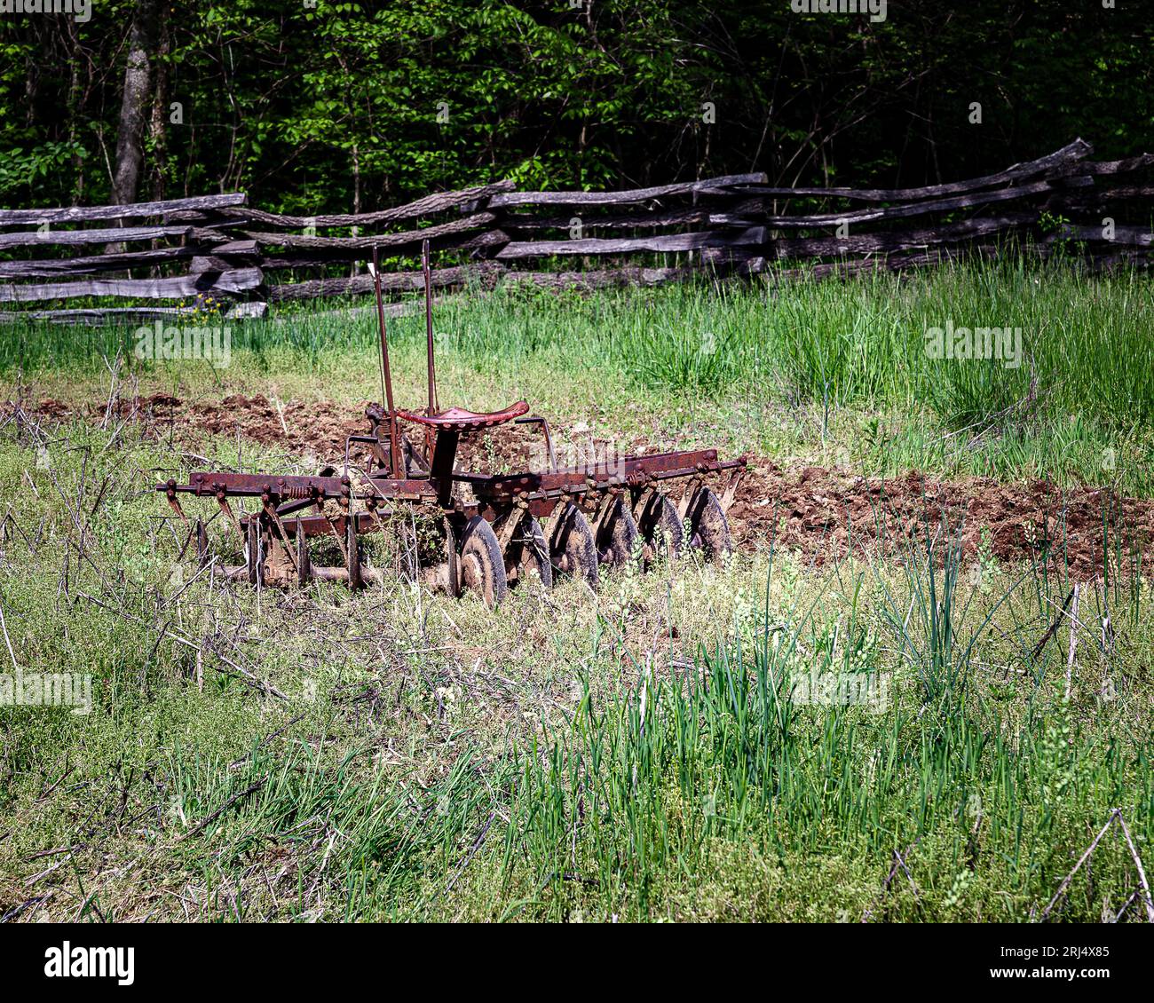 An old industrial plough in the center of a vast open field, tilling ...