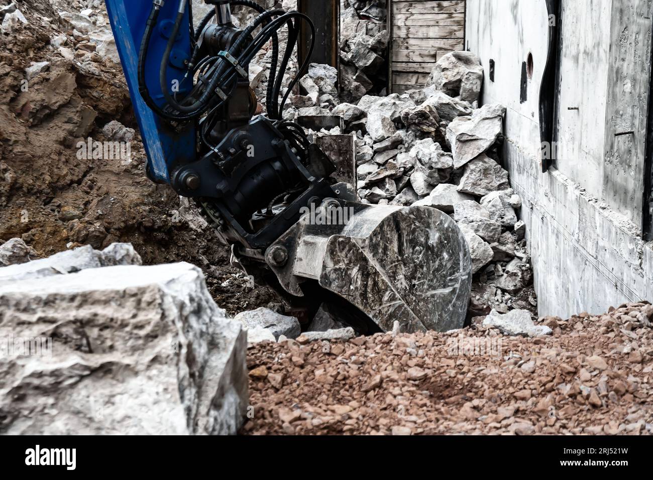 A blue digger digging a construction site with a pile of dirt and rocks ...