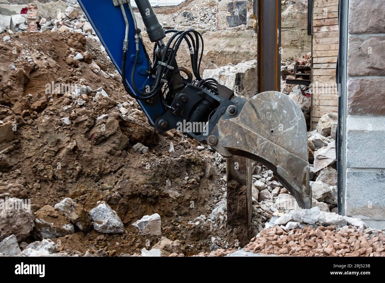A blue digger digging a construction site with a pile of dirt and rocks ...
