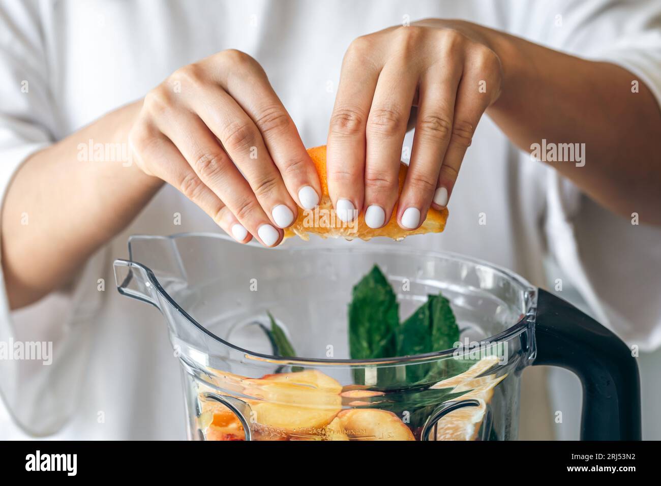 A woman squeezes orange juice into a blender, making a fruit smoothie ...