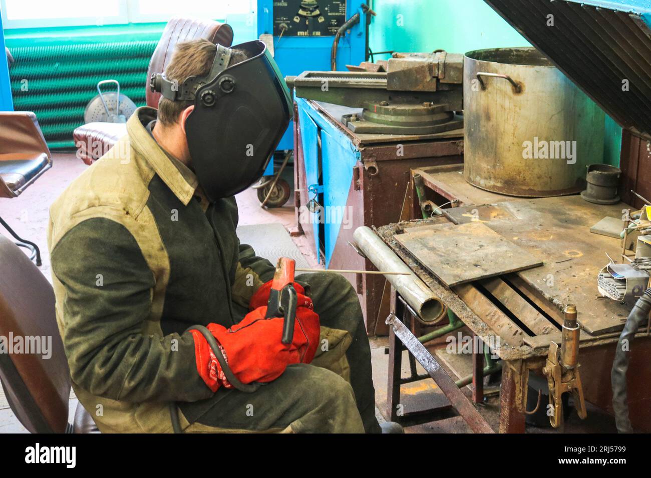 A male worker a welder in a protective mask welds a metal pipe at a ...