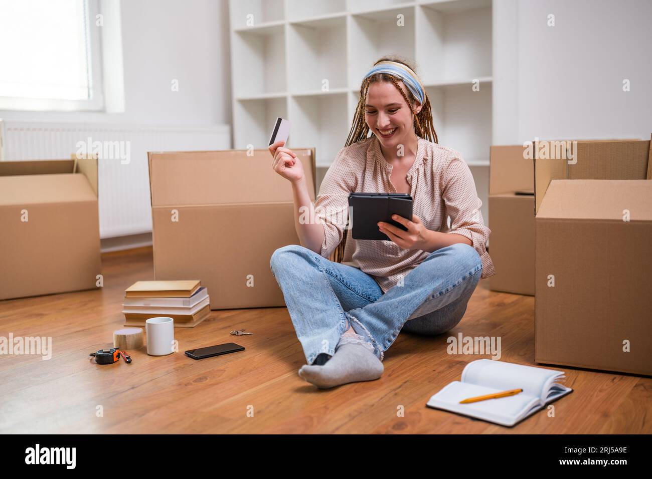 Modern ginger woman with braids using digital tablet and credit card ...