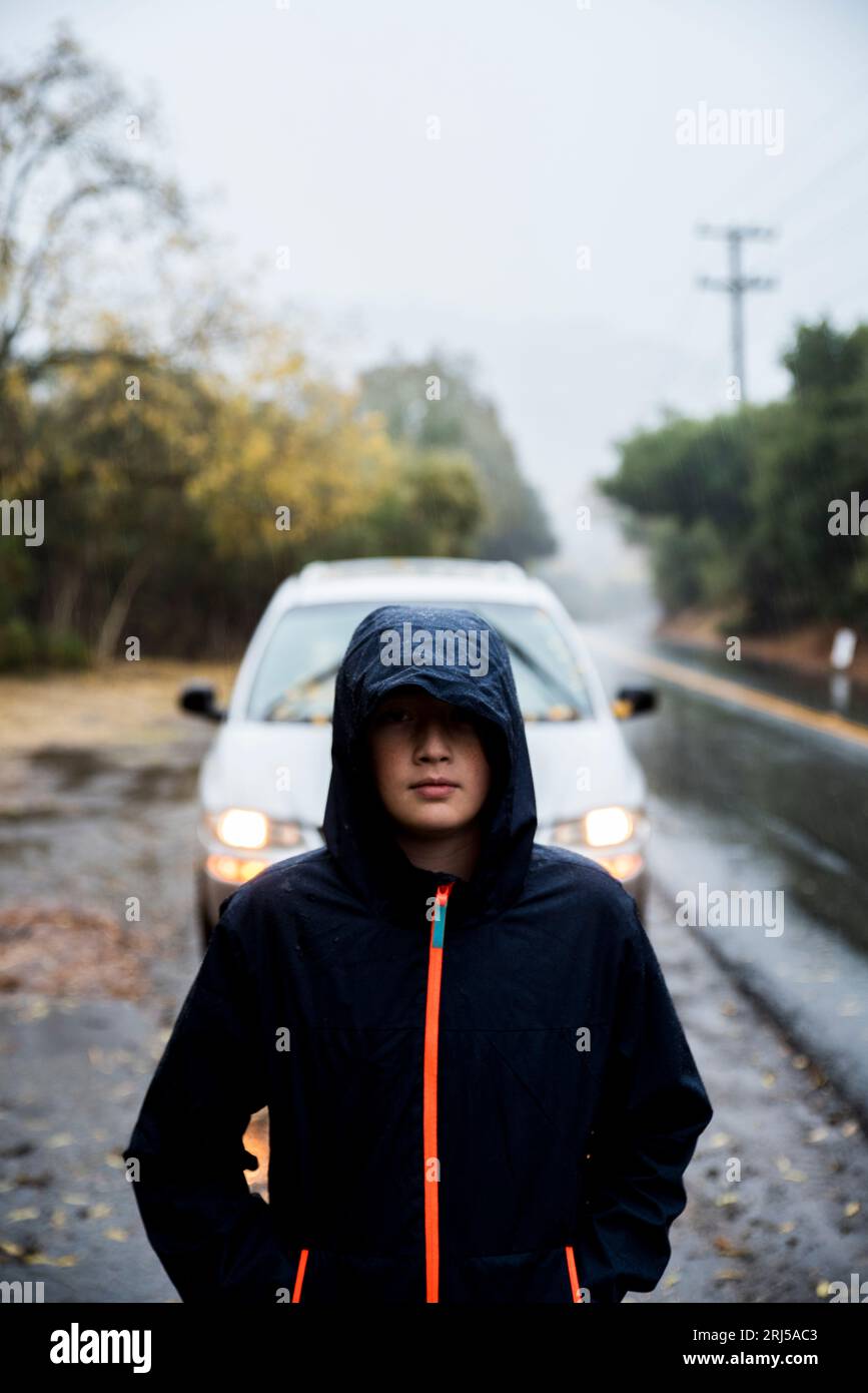 Young boy standing in front of car on side of road in rainstorm Stock ...