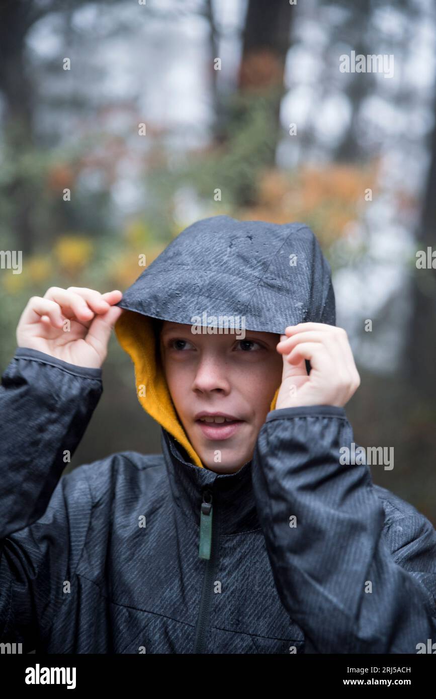 Boy pulling up rain jacket hood during rain storm Stock Photo - Alamy