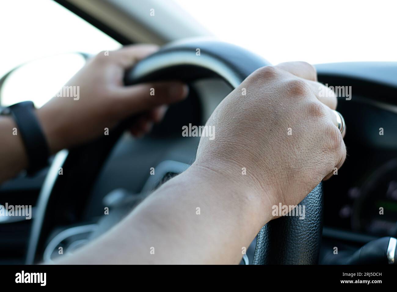 Male hands firmly hold the black steering wheel of a car. The driver ...