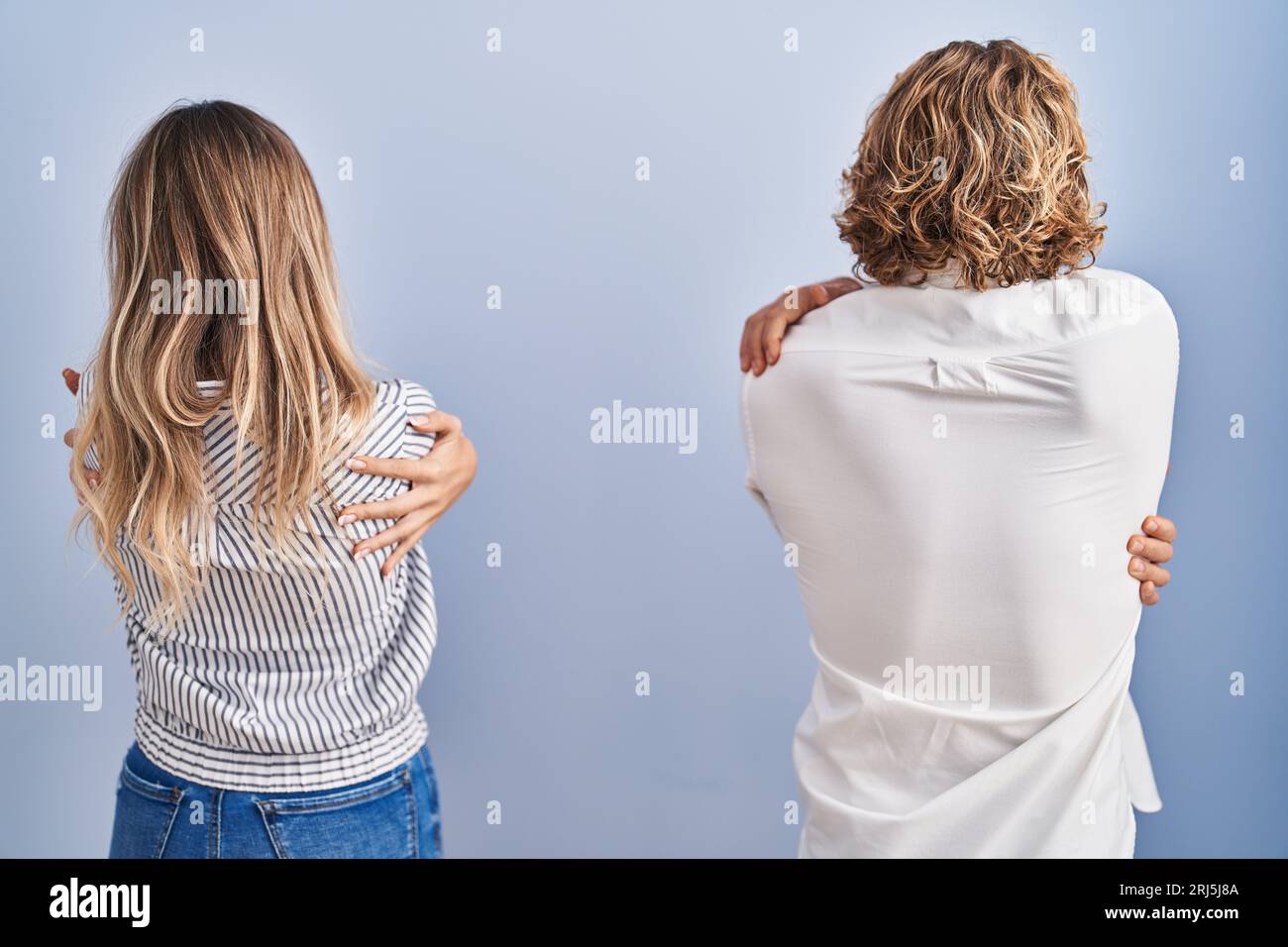 Young couple standing over blue background hugging oneself happy and ...
