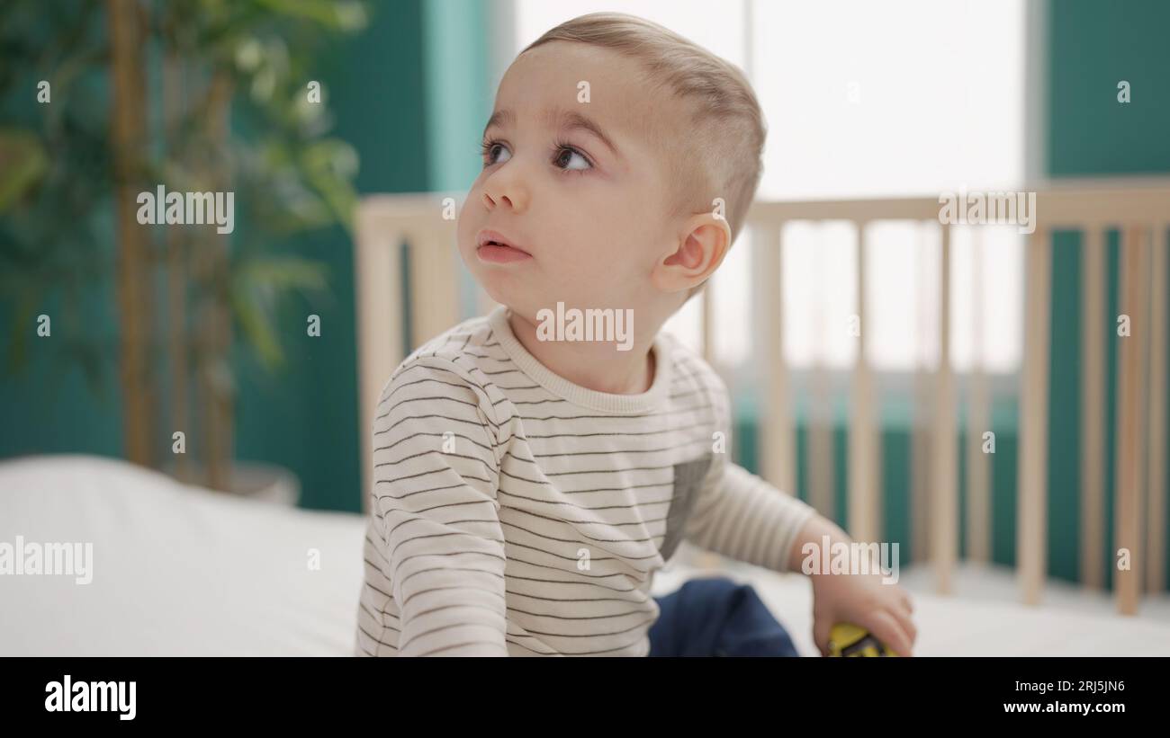 Adorable toddler sitting on bed with serious expression playing with ...