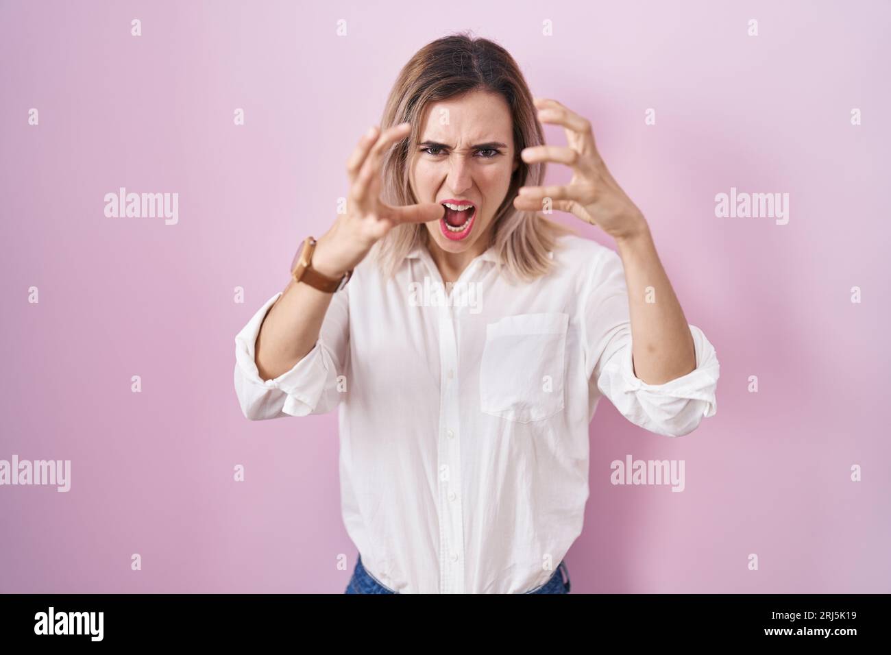 Young beautiful woman standing over pink background shouting frustrated ...