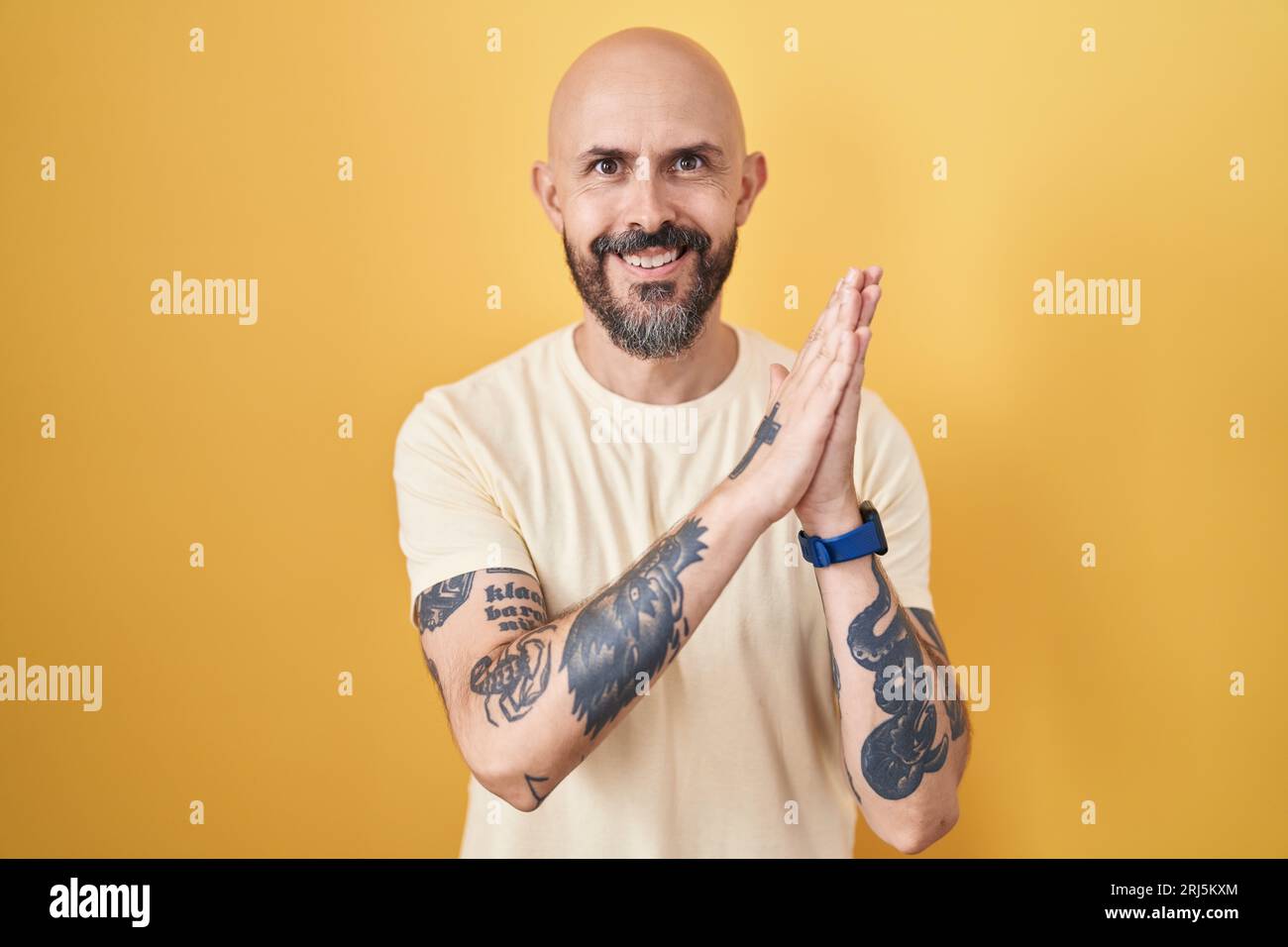 Hispanic man with tattoos standing over yellow background clapping and ...