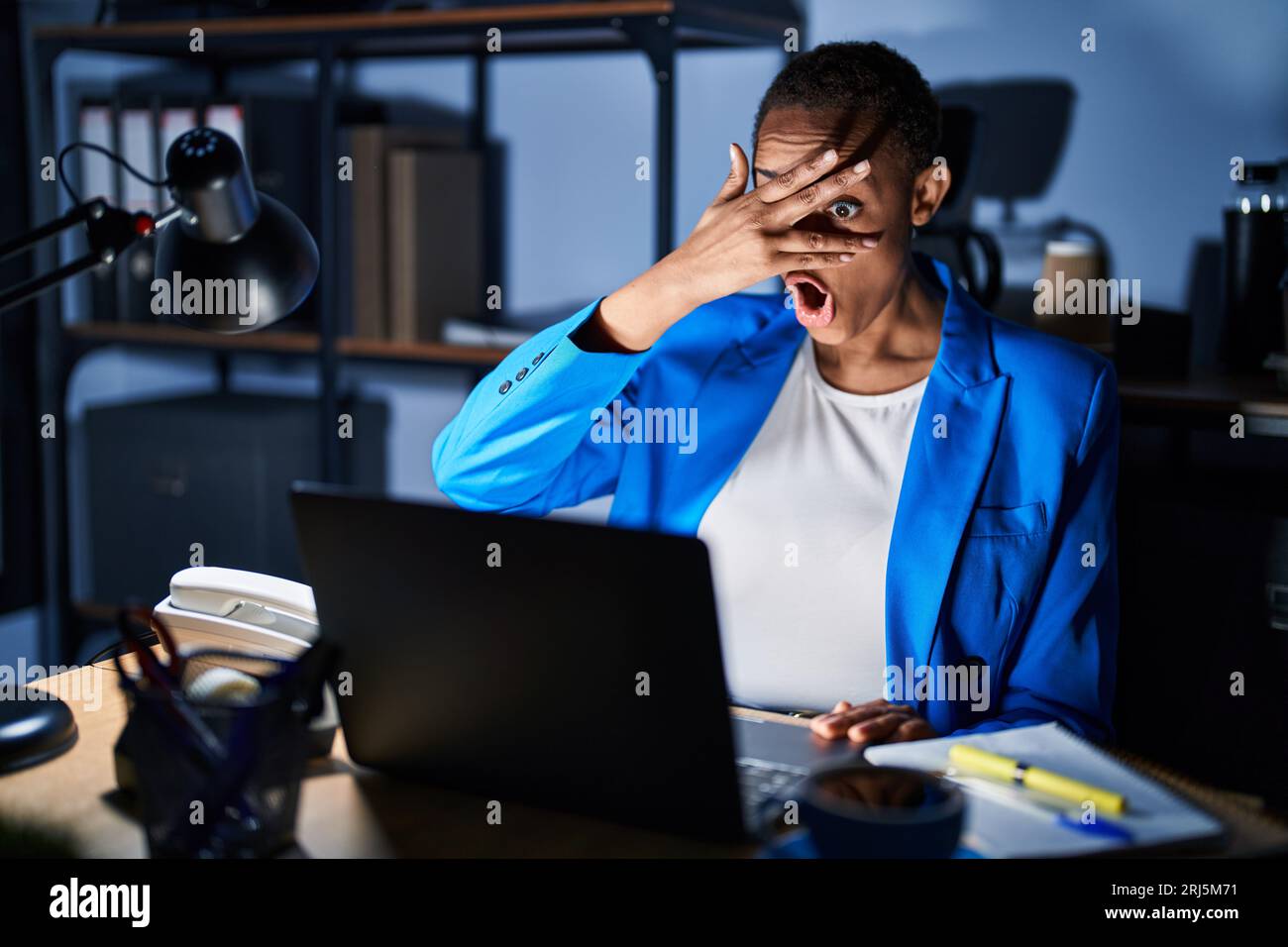 Beautiful african american woman working at the office at night peeking ...
