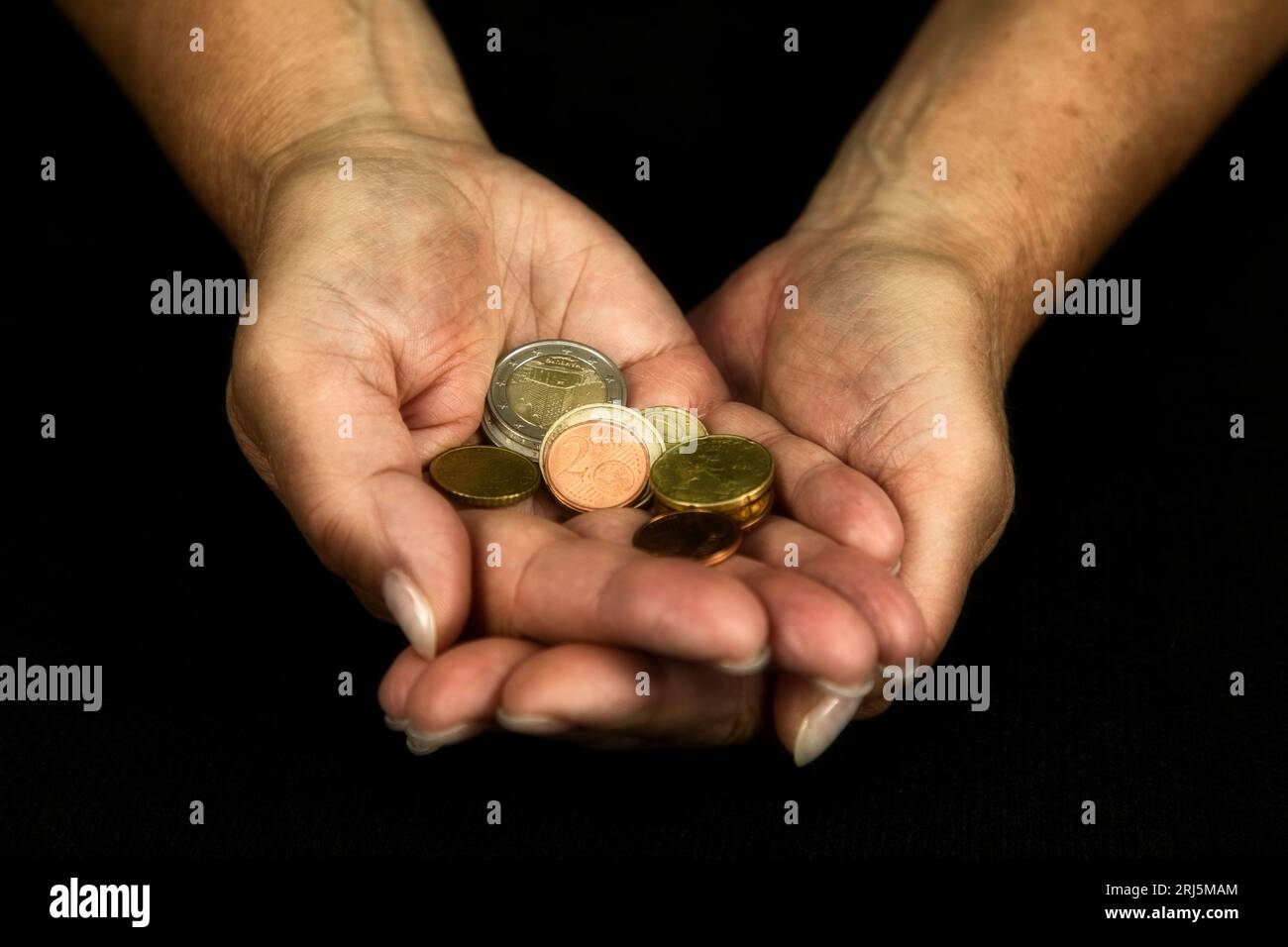 A man standing against a solid black background, holding money coins as ...