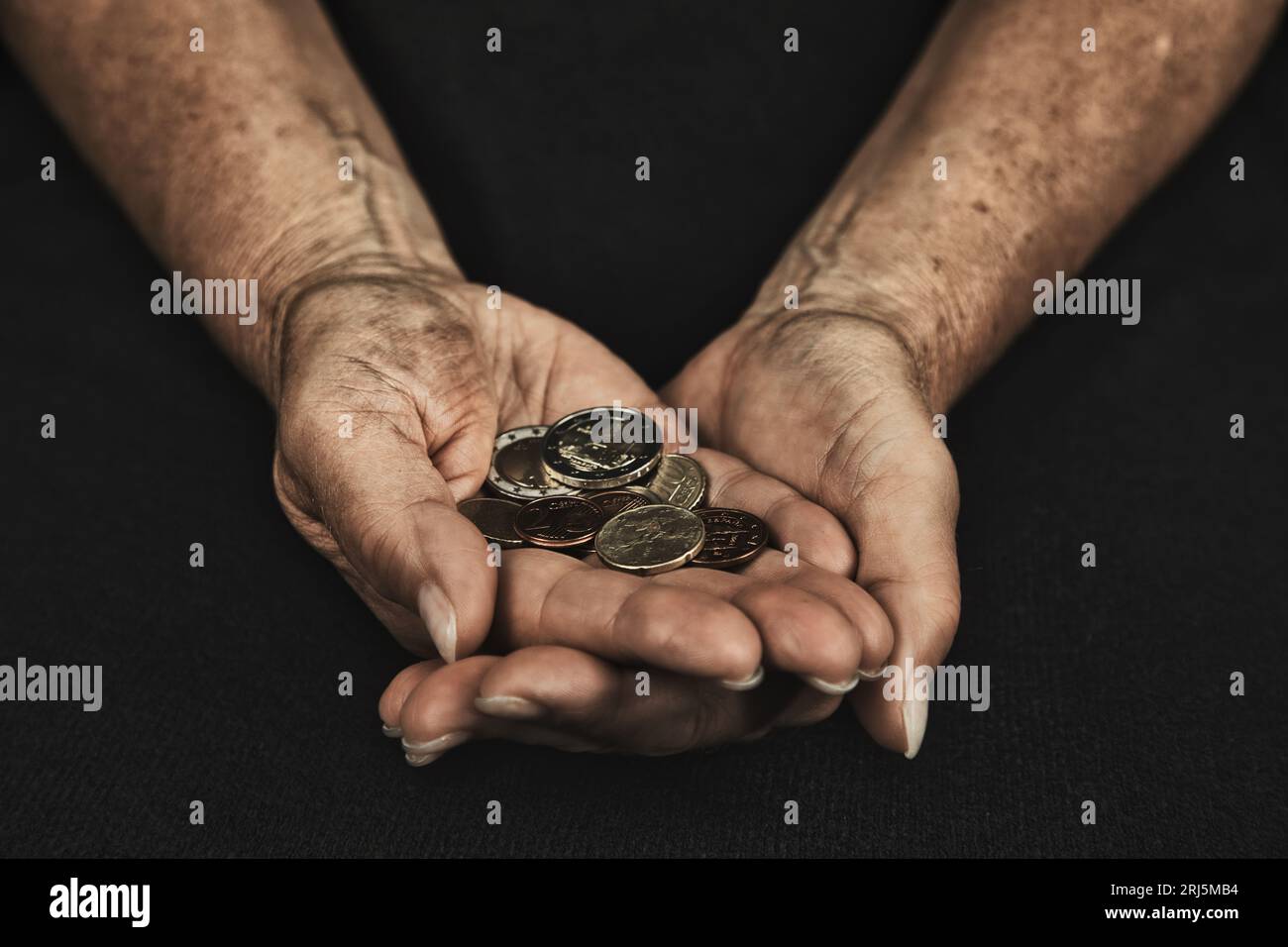 A man standing against a solid black background, holding money coins as ...