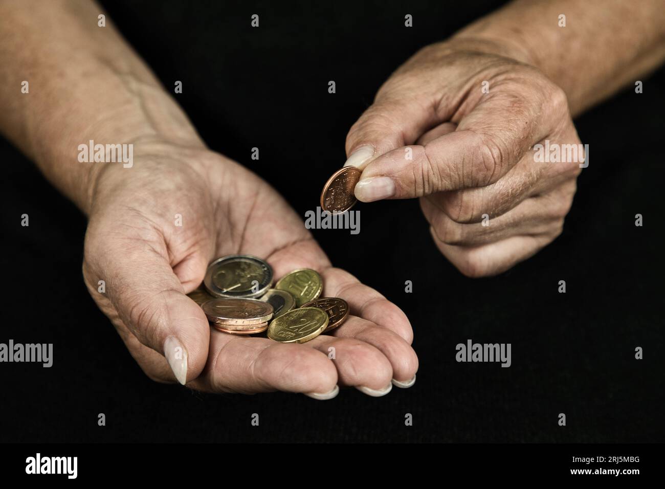 A man standing against a solid black background, holding money coins as ...