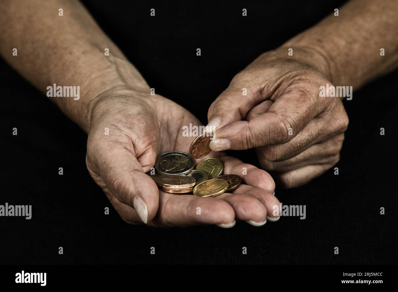 A man standing against a solid black background, holding money coins as ...