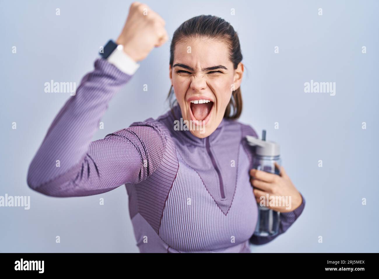 Beautiful woman wearing sportswear holding water bottle angry and mad ...