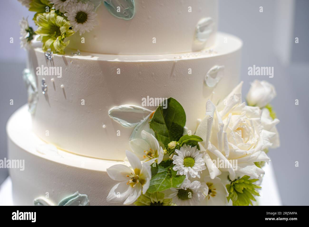 A white three-tier wedding cake adorned with white flowers Stock Photo ...