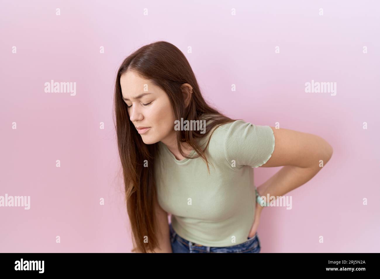 Beautiful brunette woman standing over pink background suffering of ...