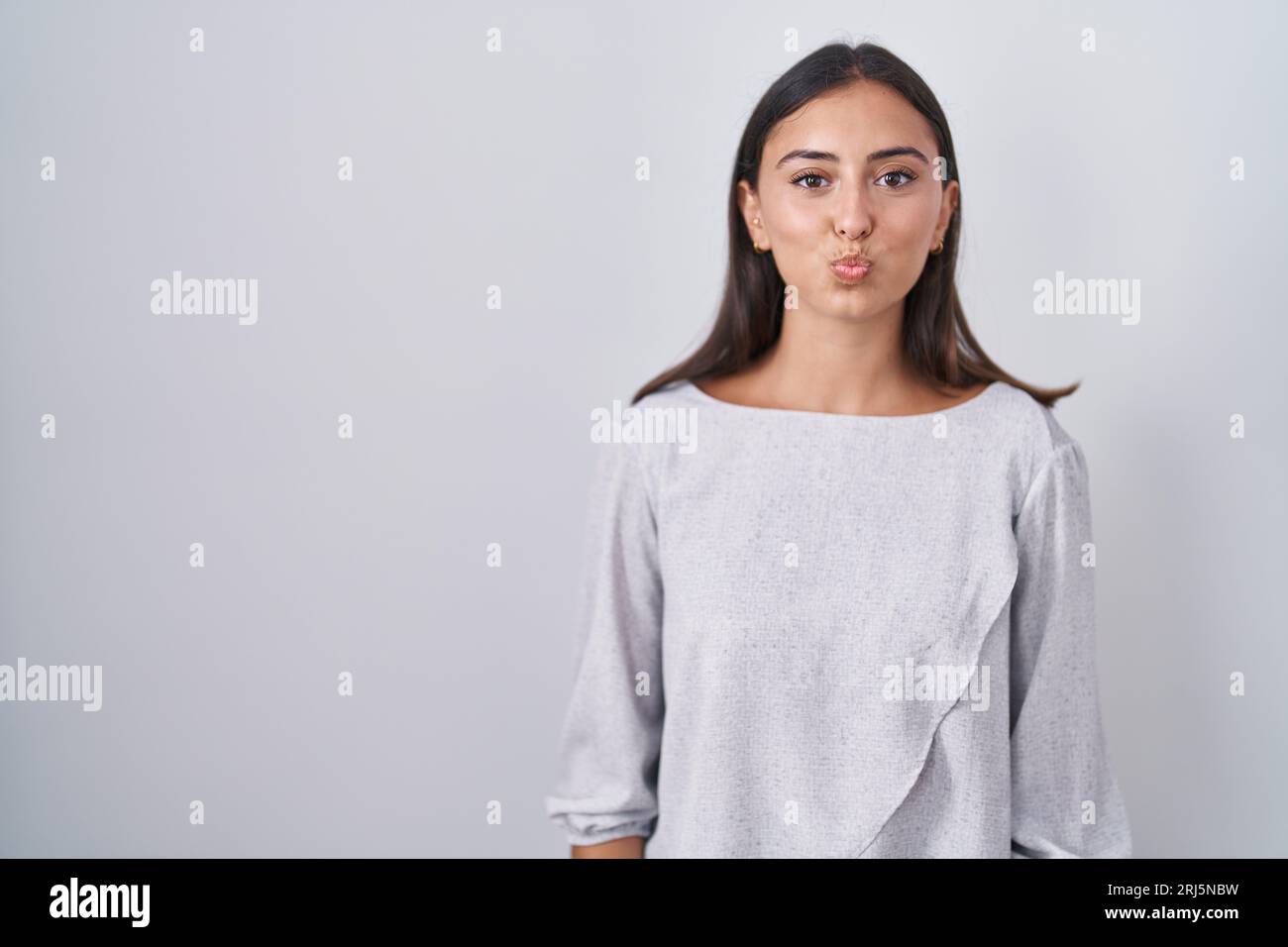 Young hispanic woman standing over white background puffing cheeks with ...