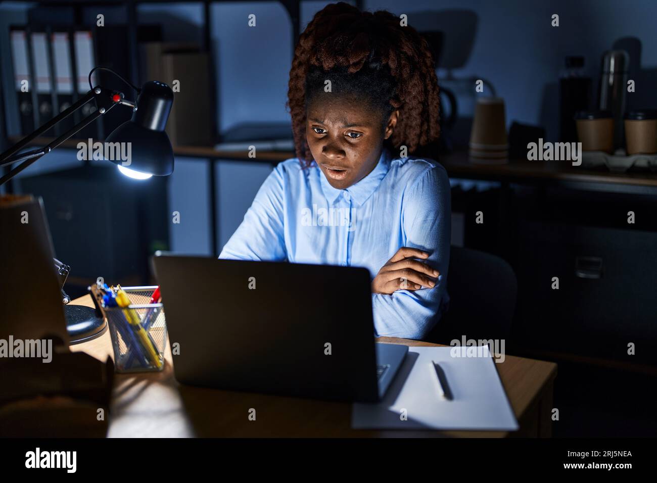 African woman working at the office at night afraid and shocked with ...
