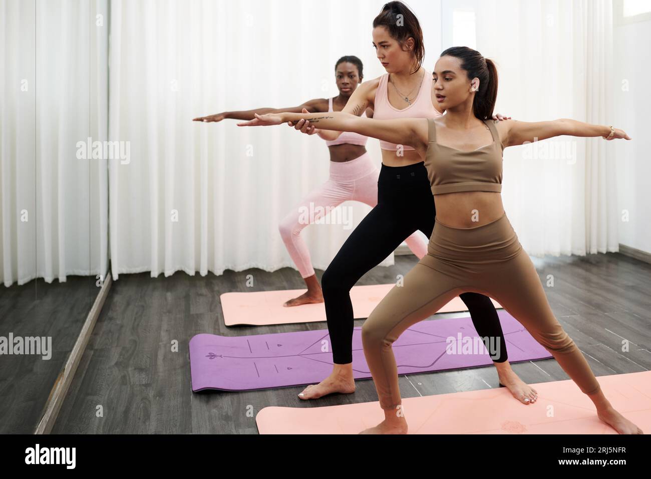 Yoga coach correcting young woman doing warrior pose in class Stock ...
