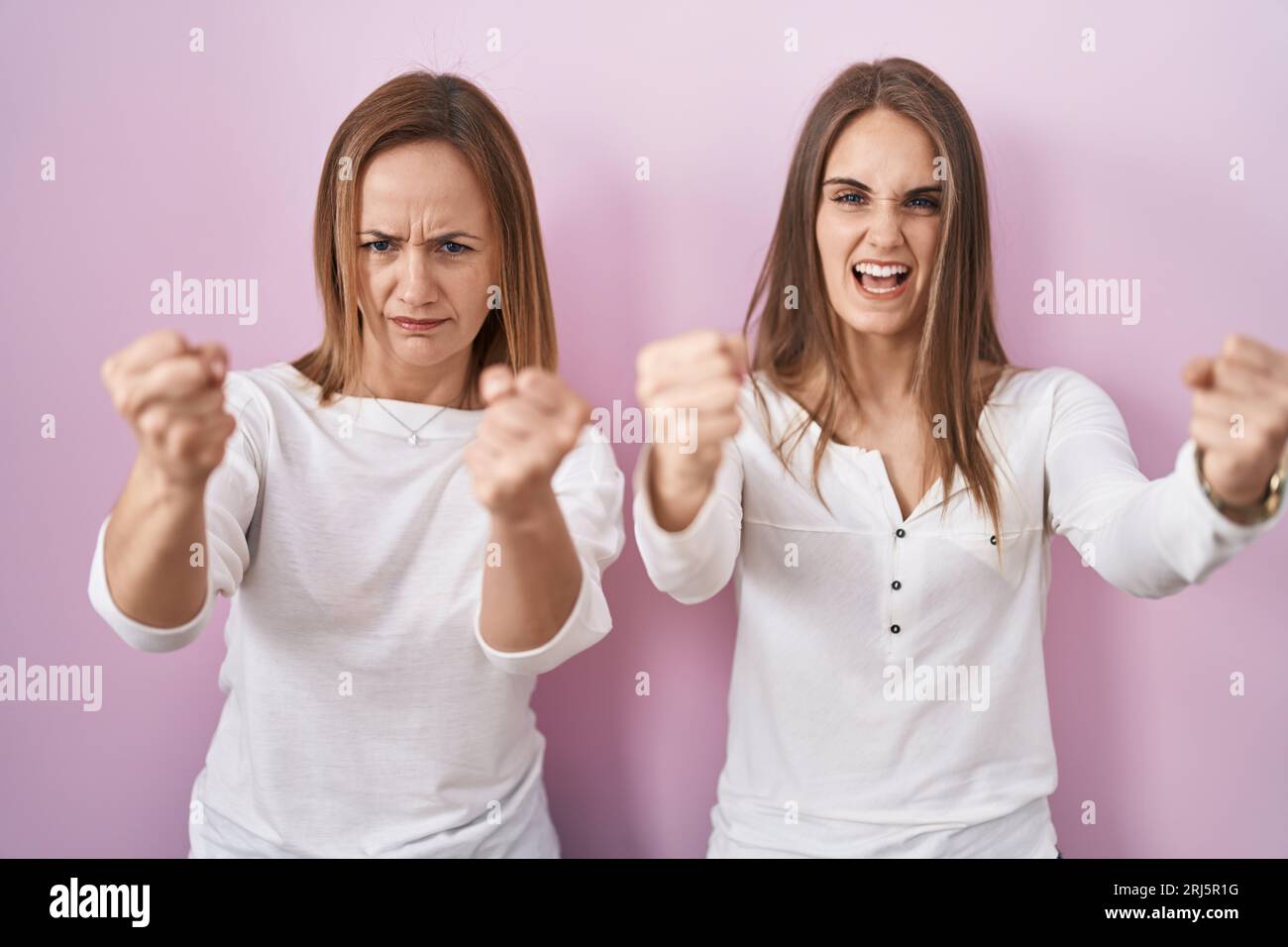 Middle age mother and young daughter standing over pink background ...