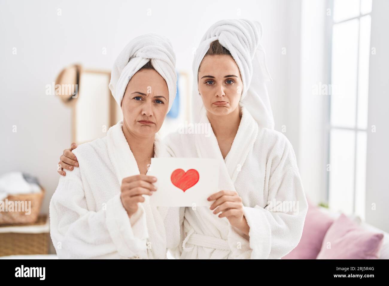 Middle age woman and daughter wearing bath robe holding heart card ...