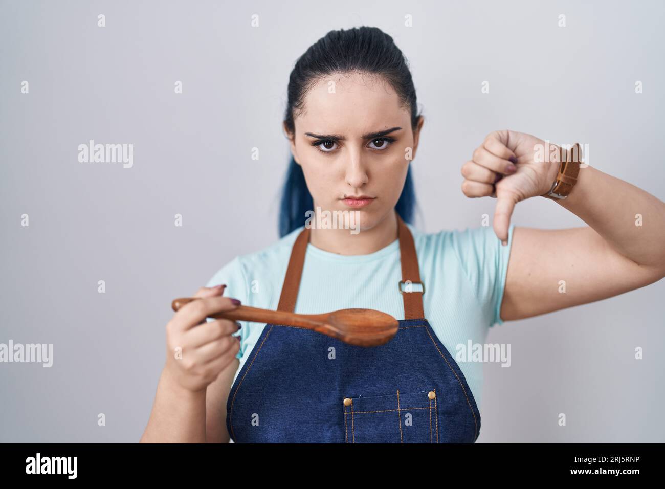 Young modern girl with blue hair wearing cook apron holding spoon with ...