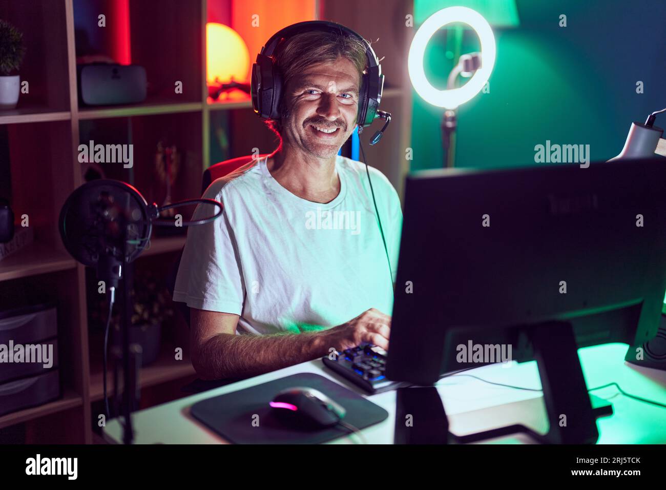 Young blond man streamer playing video game using computer at gaming ...