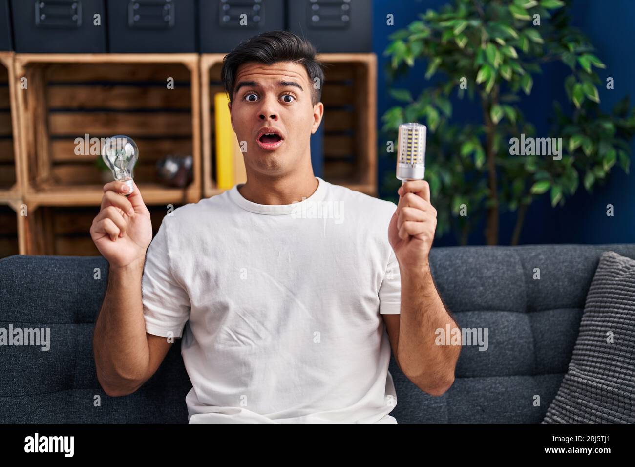Hispanic man holding led lightbulb and incandescent bulb in shock face ...