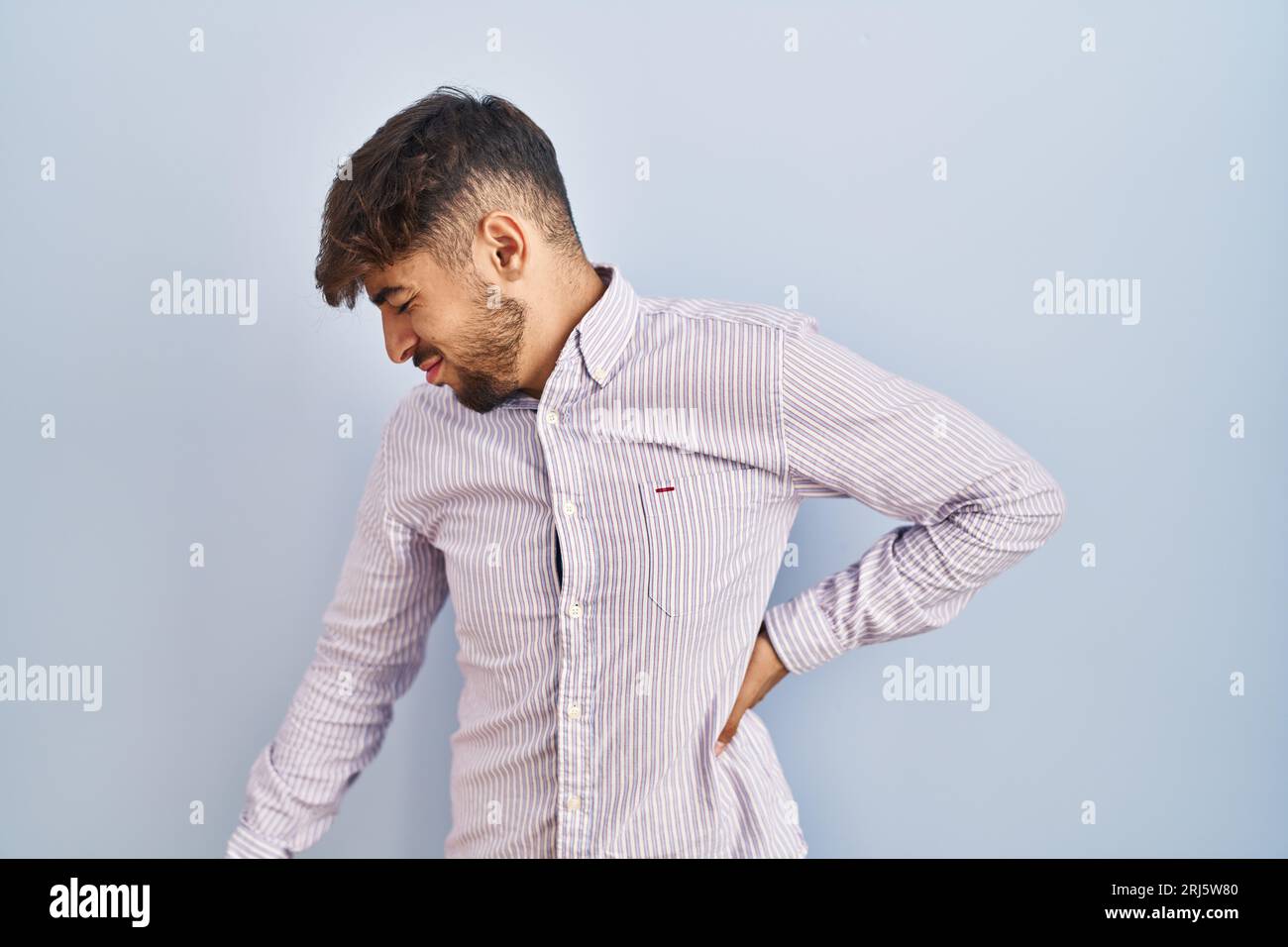 Arab man with beard standing over blue background suffering of backache ...