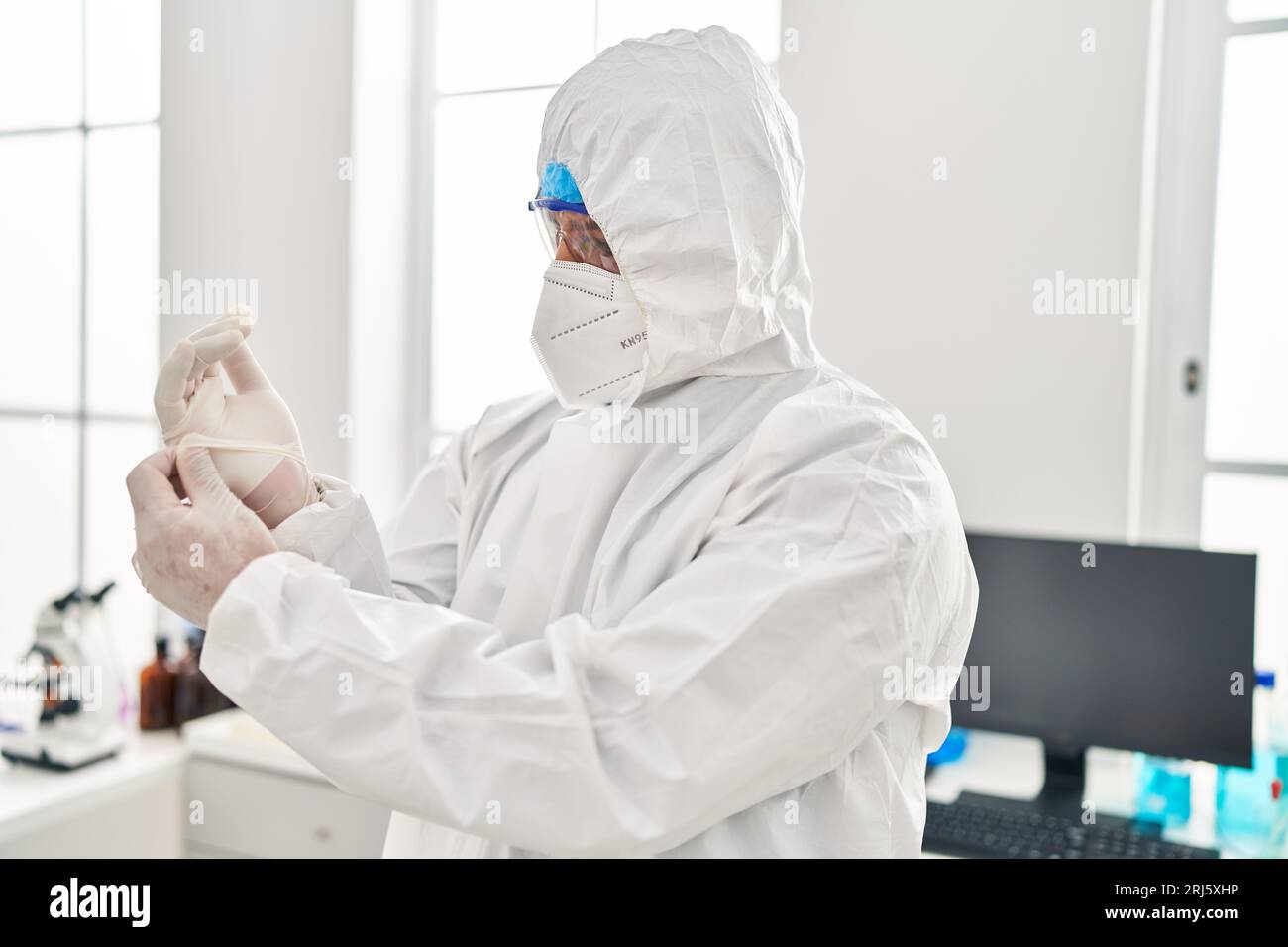 Young latin man scientist wearing covid protection uniform and gloves ...