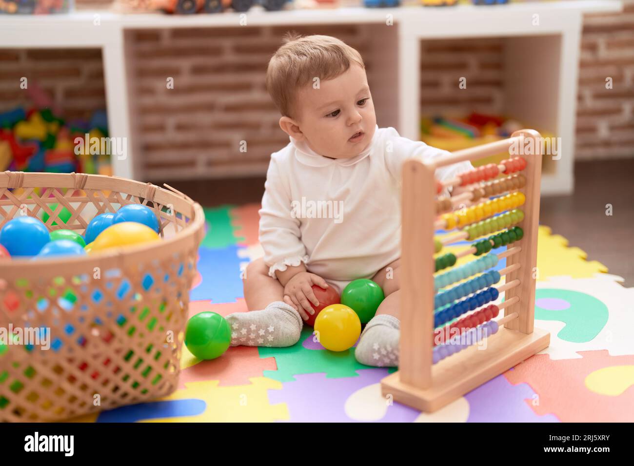 Adorable toddler playing with abacus sitting on floor at kindergarten ...