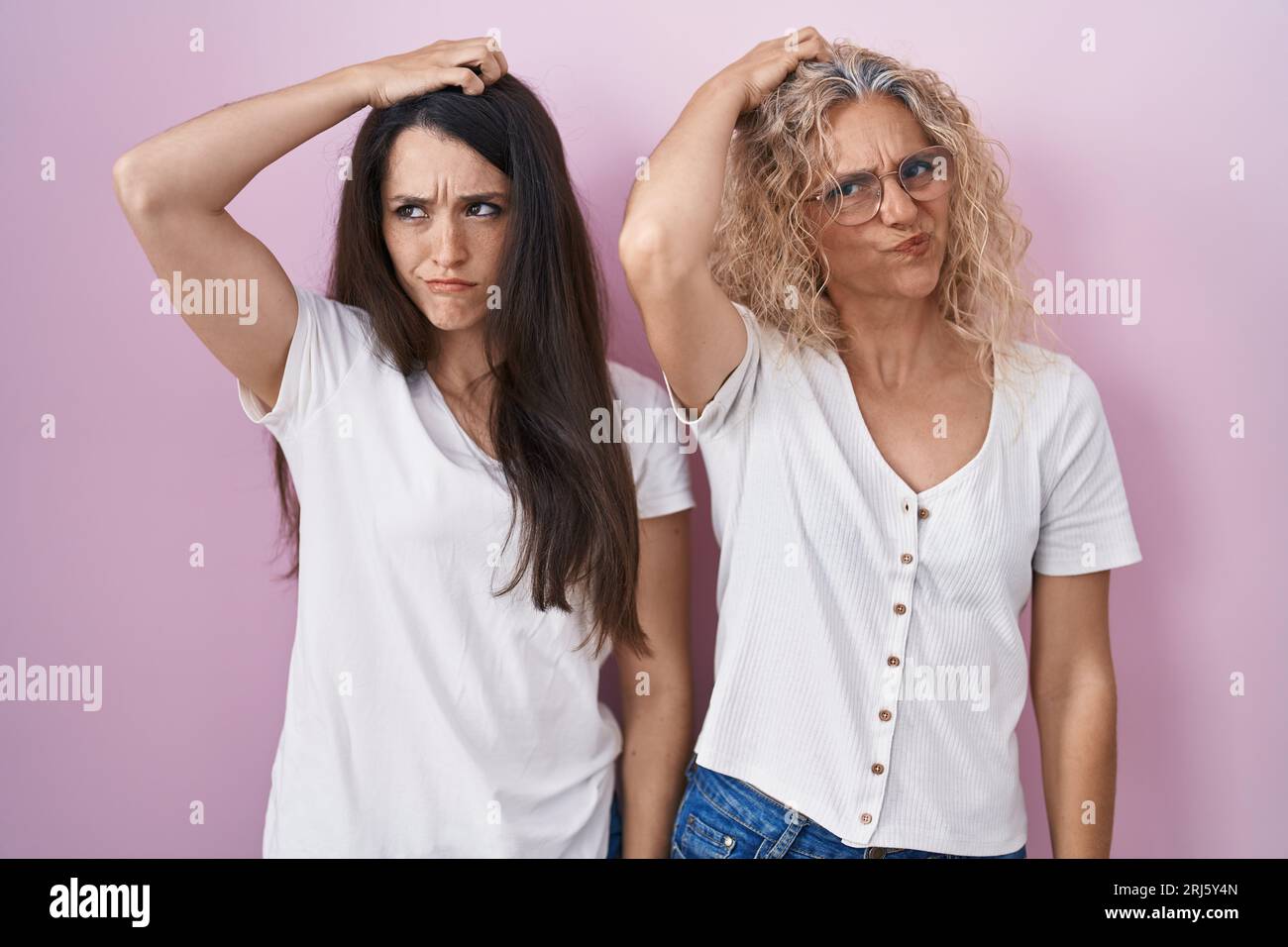Mother and daughter standing together over pink background confuse and ...