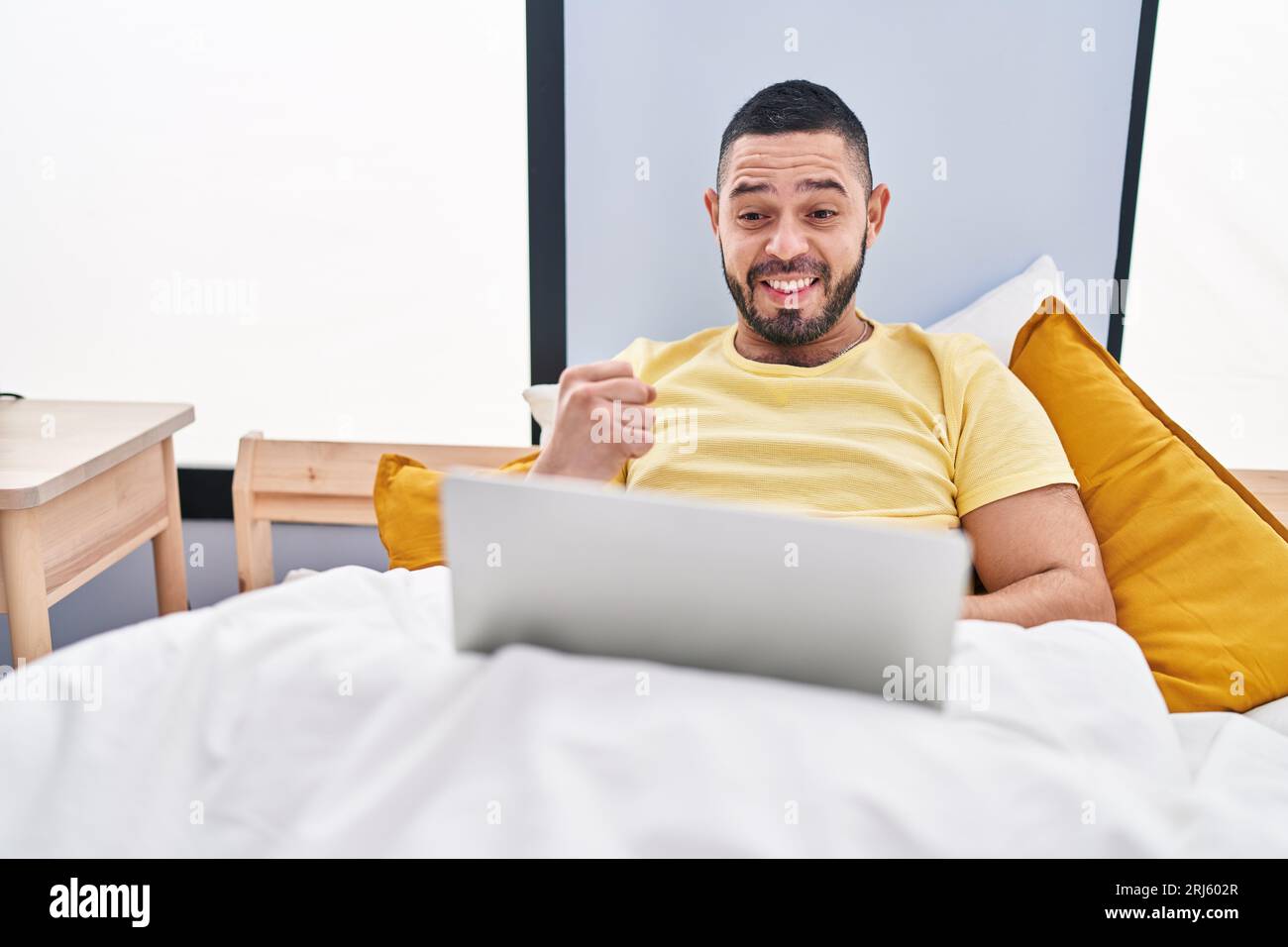 Hispanic man using laptop on the bed celebrating achievement with happy ...
