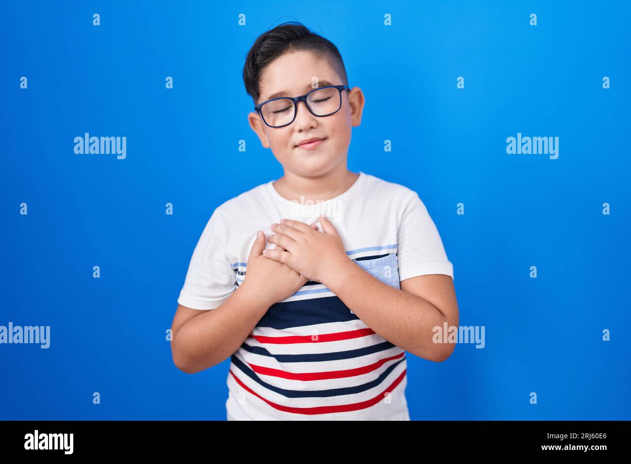Young hispanic kid standing over blue background smiling with hands on ...