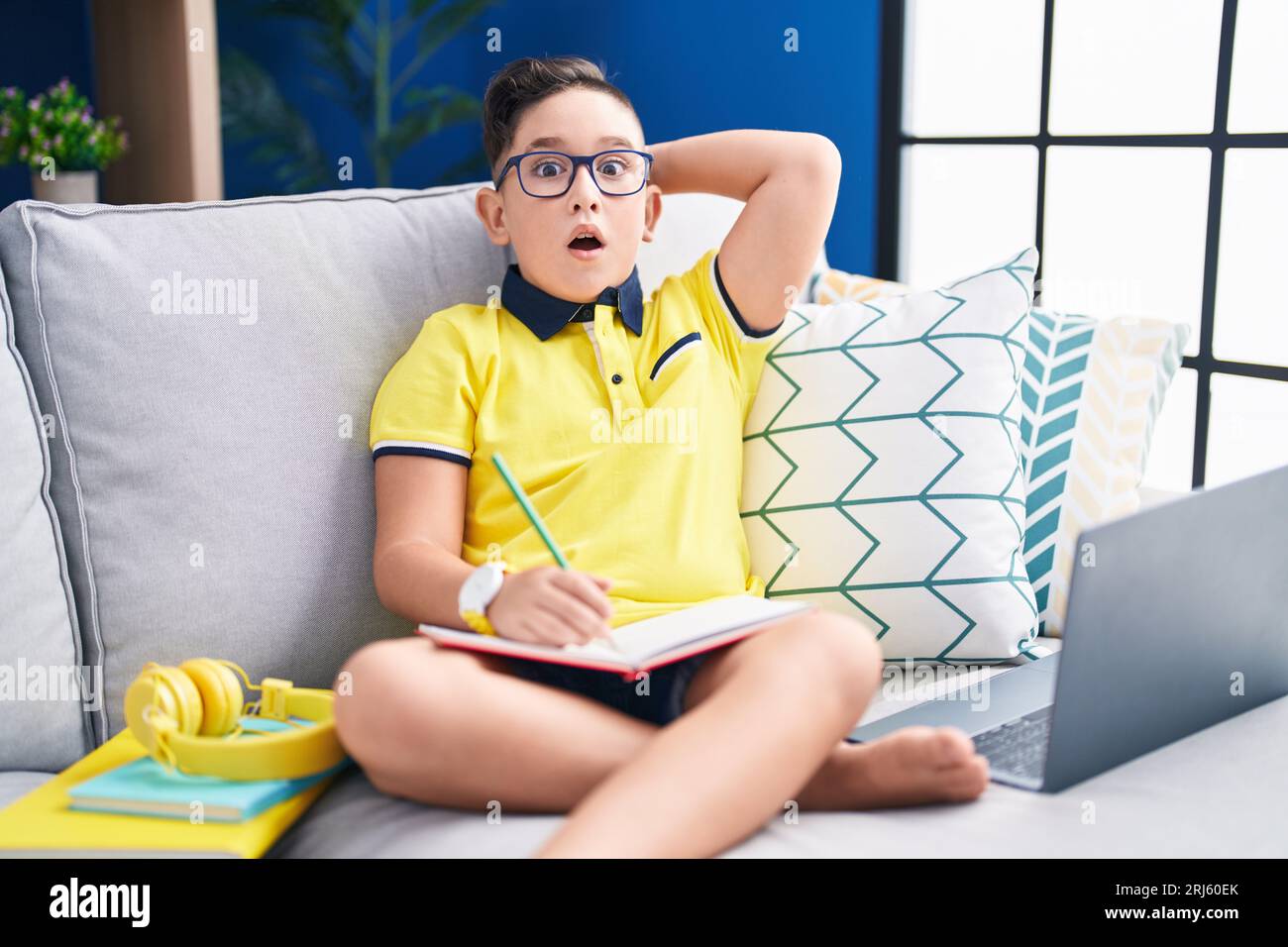 Young hispanic kid doing homework sitting on the sofa crazy and scared ...