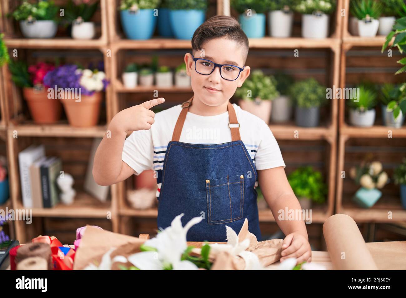 Young hispanic kid working at florist shop smiling happy pointing with ...