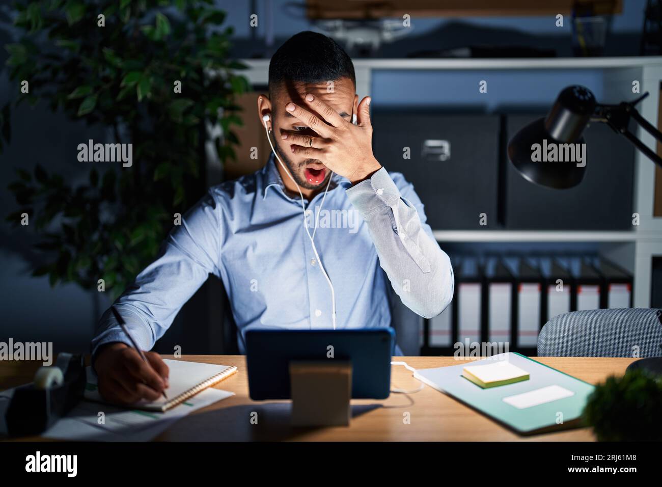 Young hispanic man working at the office at night peeking in shock ...