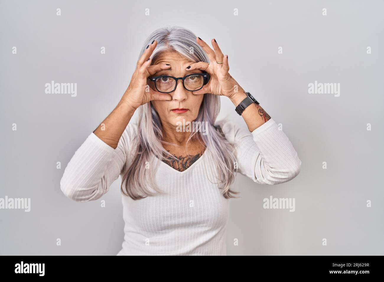 Middle age woman with grey hair standing over white background trying ...