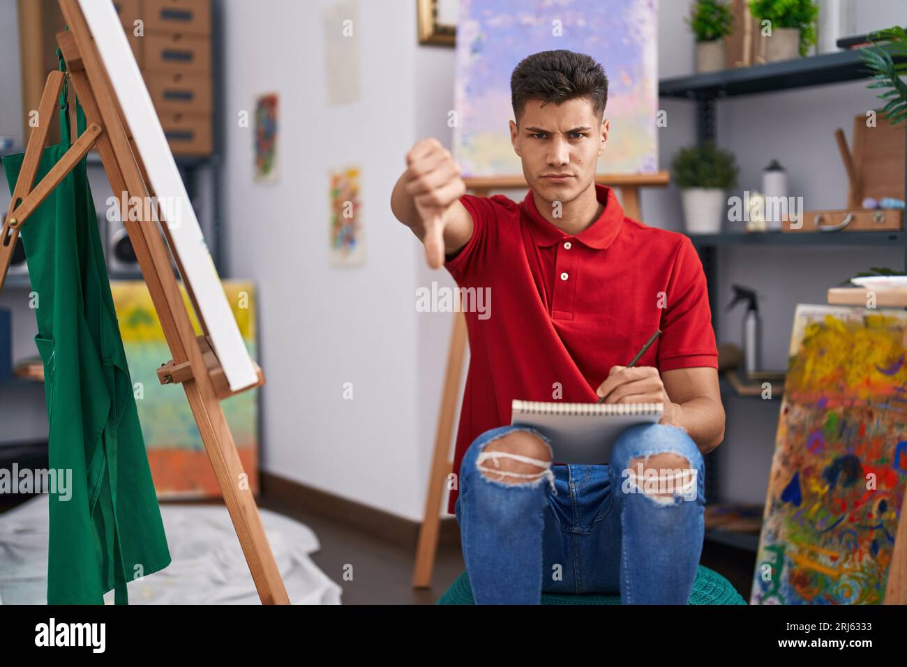 Young hispanic man drawing on art notebook with angry face, negative ...