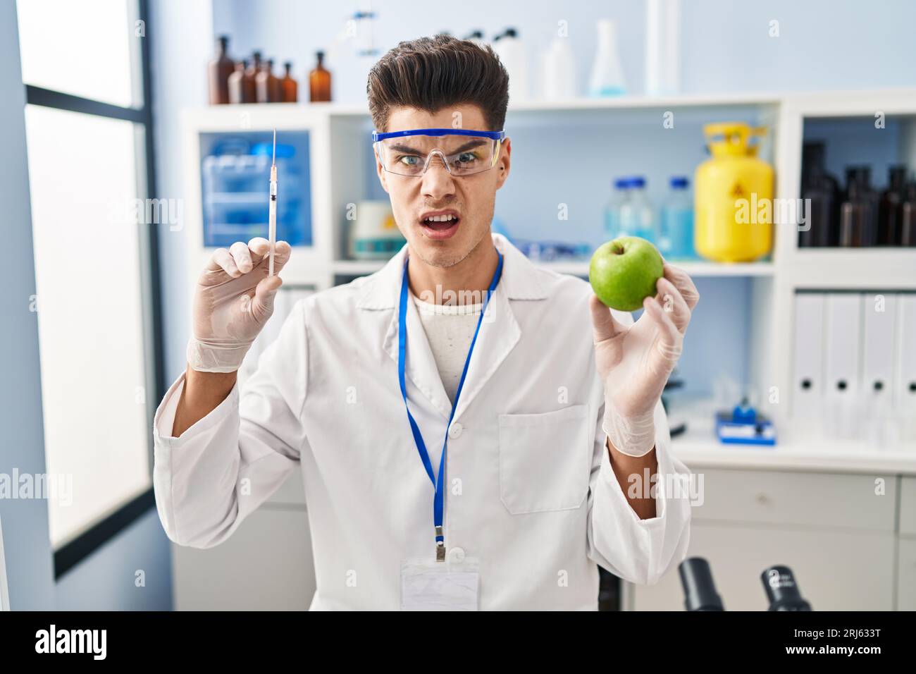 Young hispanic man working at scientist laboratory holding apple in ...