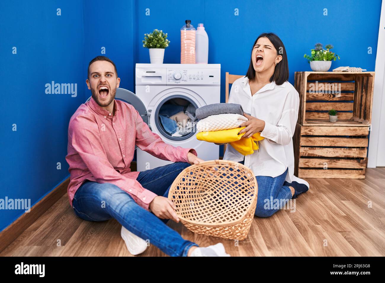 Young couple doing laundry at home angry and mad screaming frustrated ...