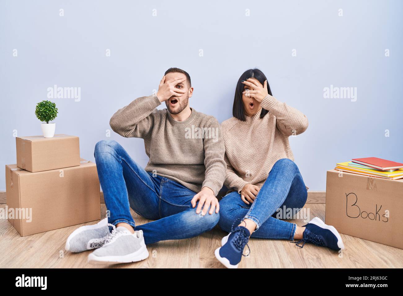 Young couple moving to a new home peeking in shock covering face and ...