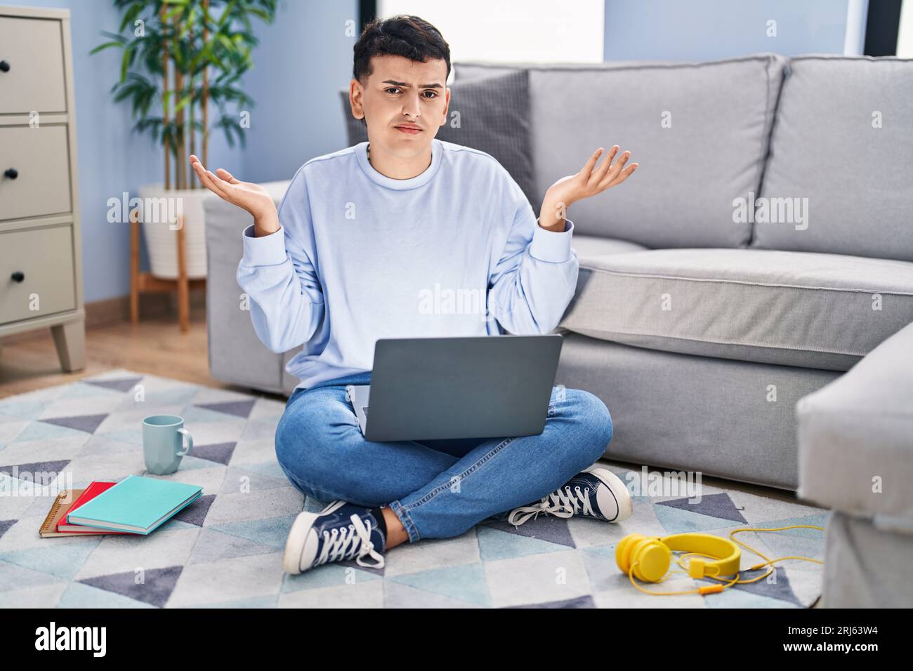 Non binary person studying using computer laptop sitting on the floor ...