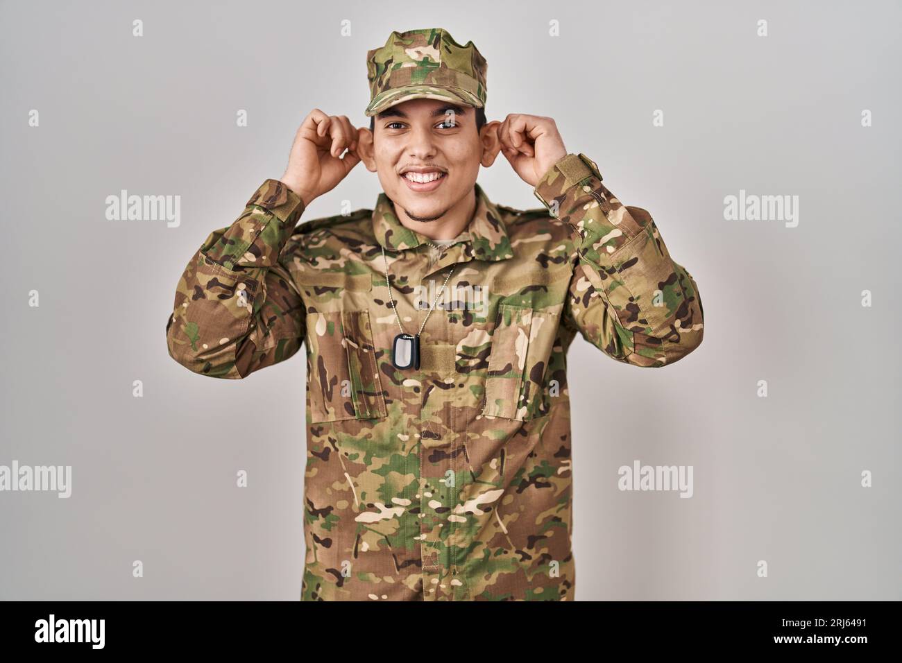Young arab man wearing camouflage army uniform smiling pulling ears ...